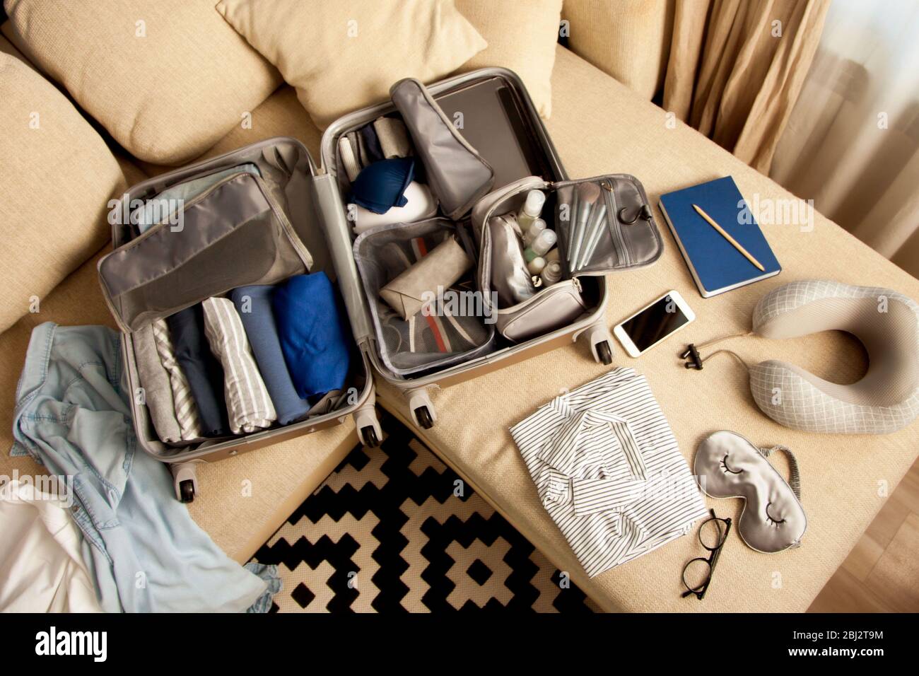 Open grey suitcase with different clothes packed for journey at home ...