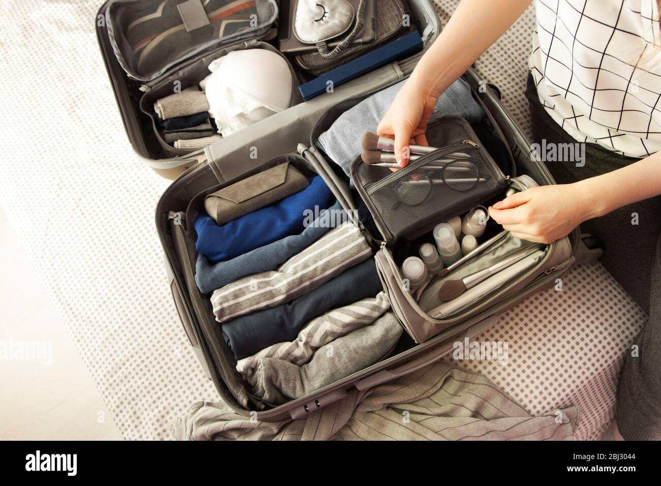 Open grey suitcase with different clothes packed for journey at home ...
