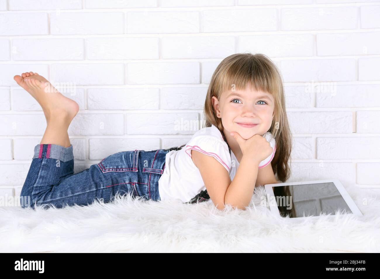 Little girl with tablet on brick wall background Stock Photo - Alamy