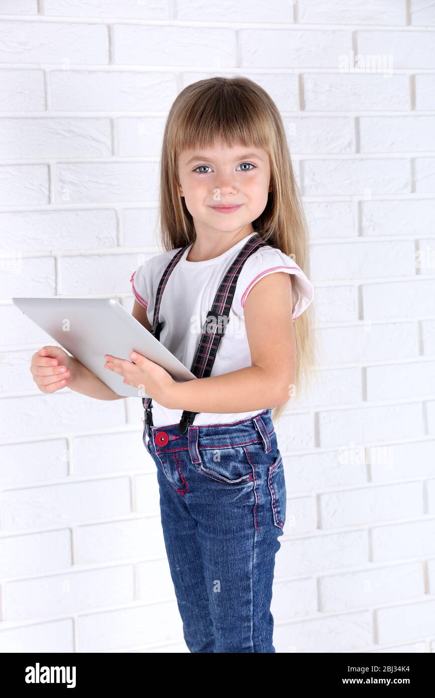 Little girl with tablet on brick wall background Stock Photo - Alamy