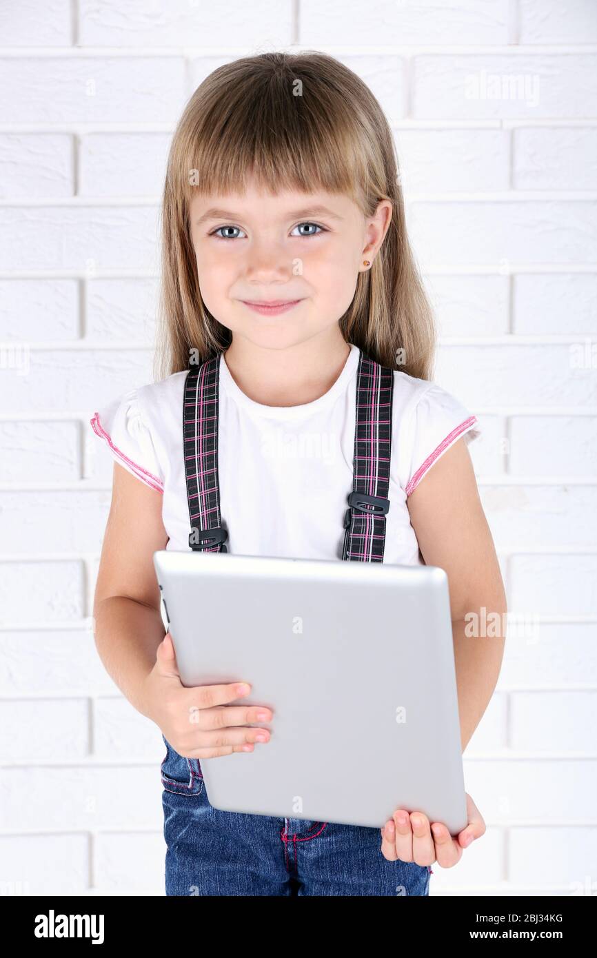 Little girl with tablet on brick wall background Stock Photo - Alamy