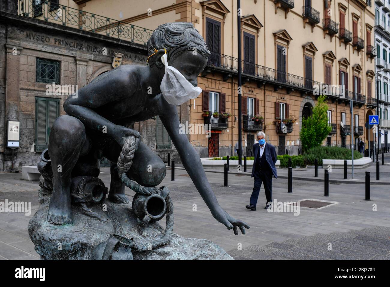 Man passes a statue of a child fisherman with protective mask, in ...