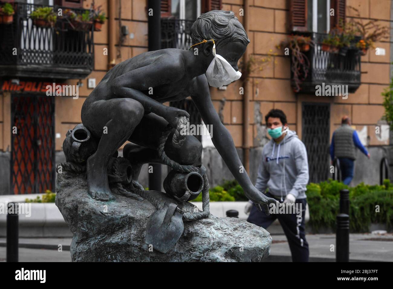 Man passes a statue of a child fisherman with protective mask, in ...