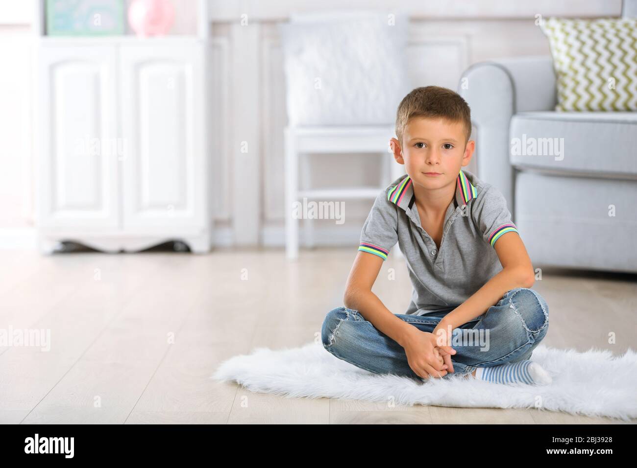Little boy sitting on carpet, on home interior background Stock Photo ...