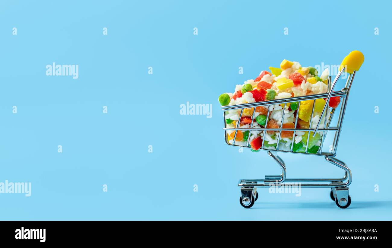 Frozen vegetables assorted in toy shopping cart on blue background ...