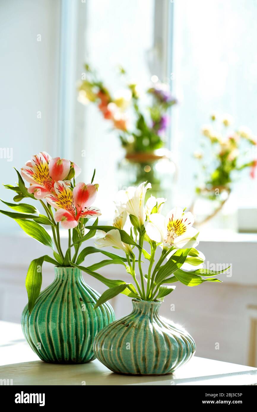 Beautiful Alstroemeria flowers in aquamarine vases on window background ...