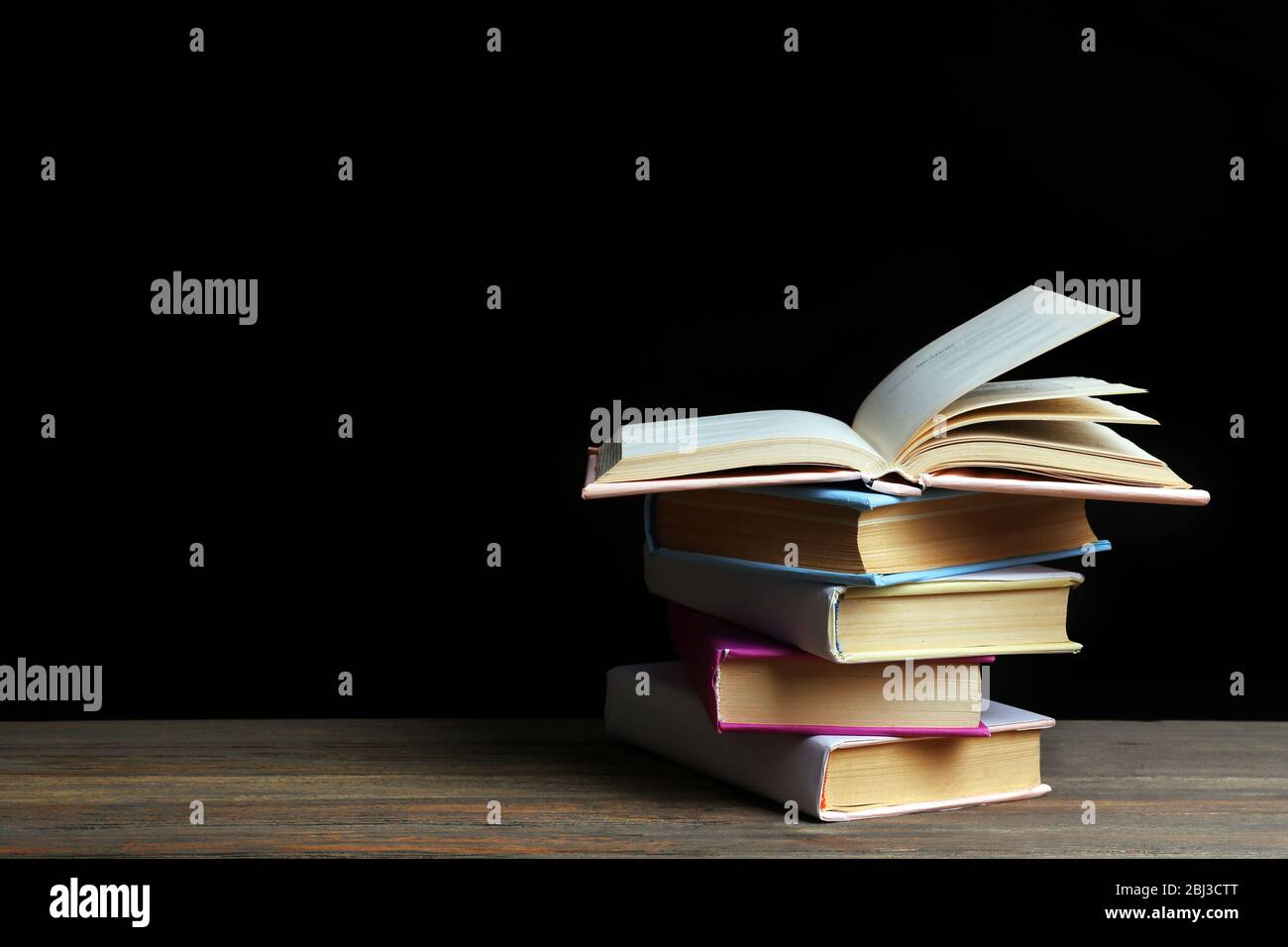Pile of different books on wooden table against black background Stock ...