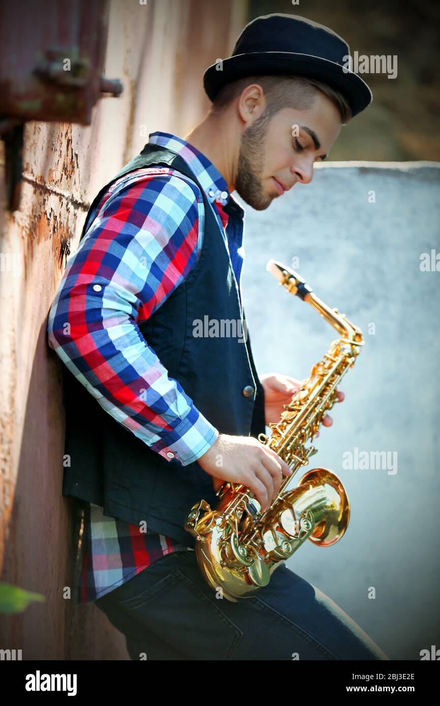 Young man playing on saxophone outside near the old wall Stock Photo ...