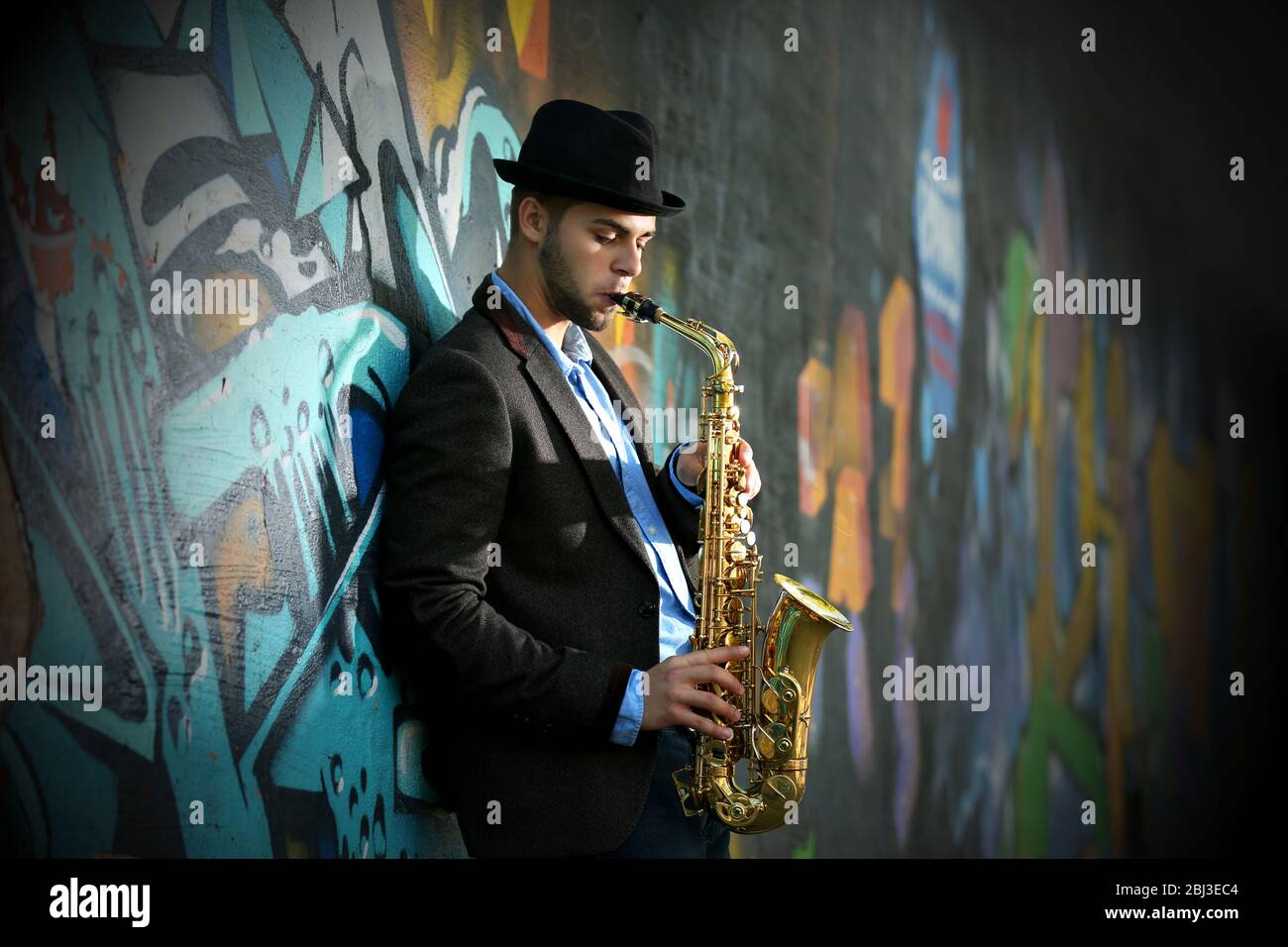 Young man with saxophone outside near the old painted wall Stock Photo ...