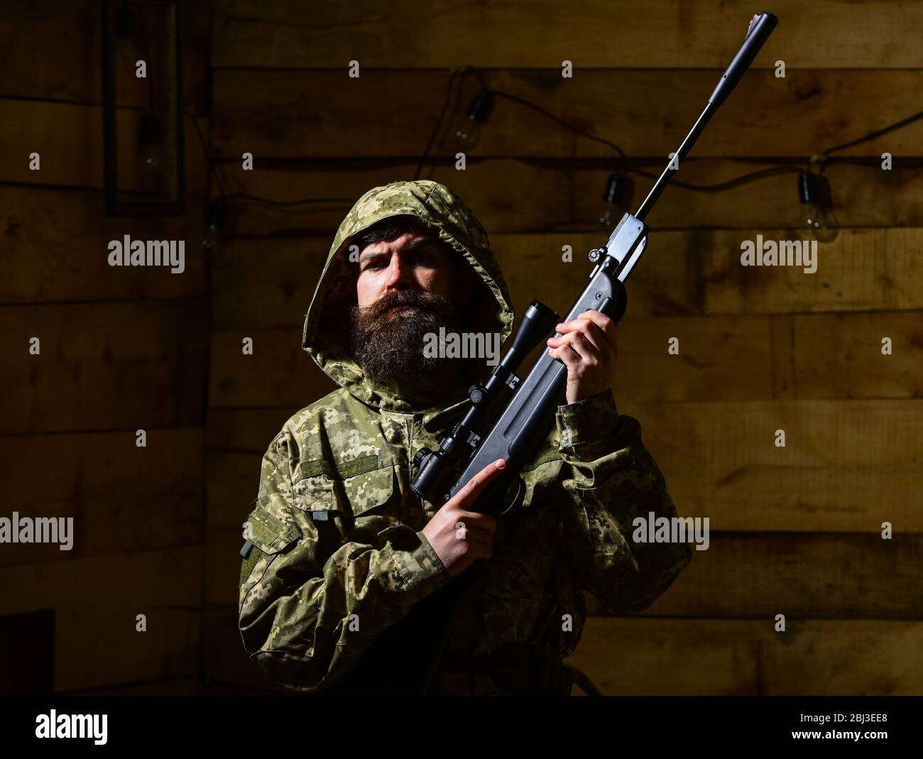 Man with beard wears camouflage hooded clothing, wooden interior ...