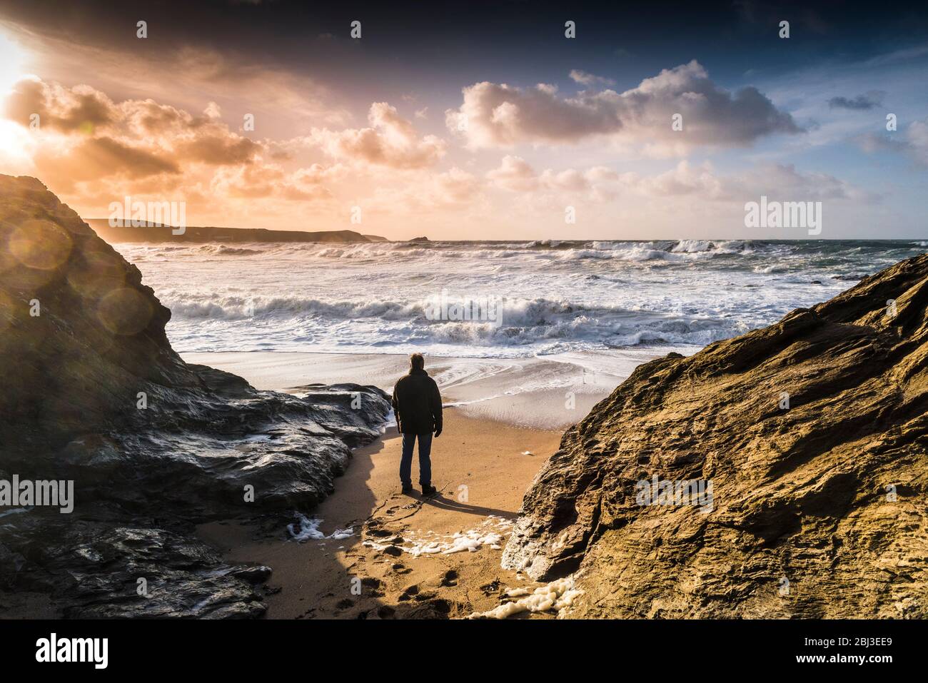 A man standing alone on the beach and watching the incoming waves in a ...