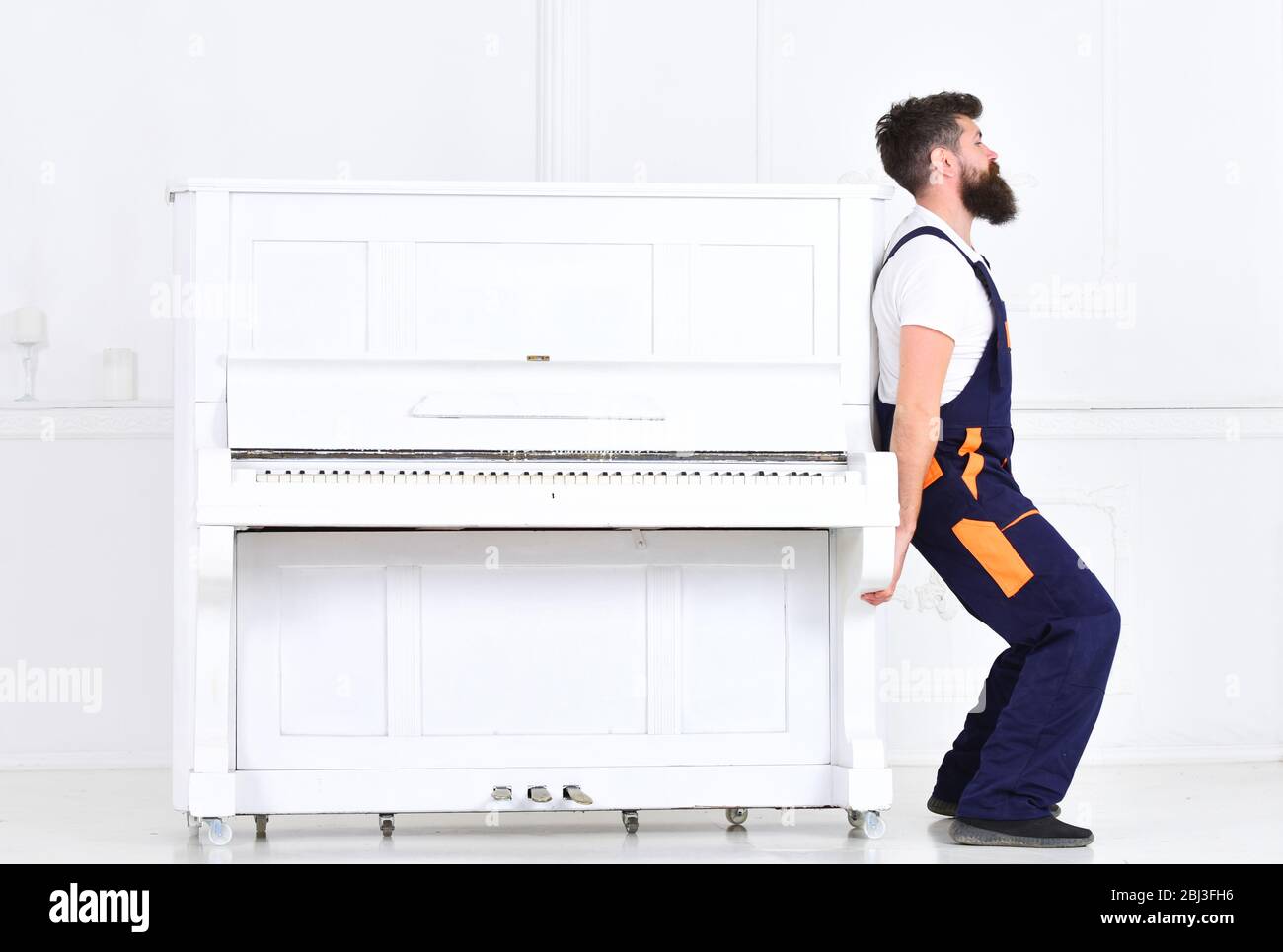 Handsome bearded strong man lifting old wooden piano with open keyboard ...