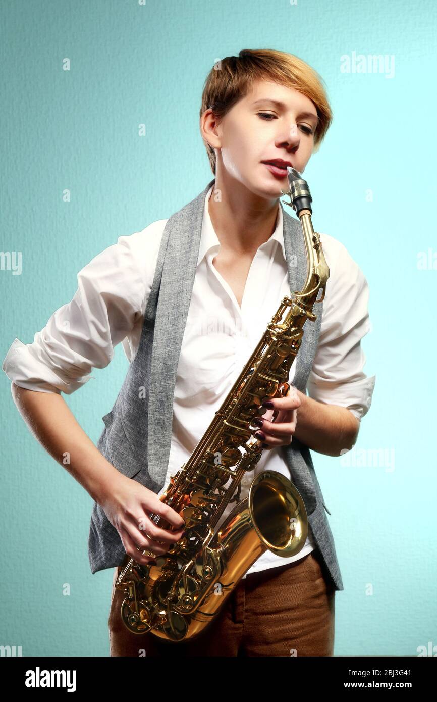 Pretty woman plays music on saxophone in front of blue background Stock ...
