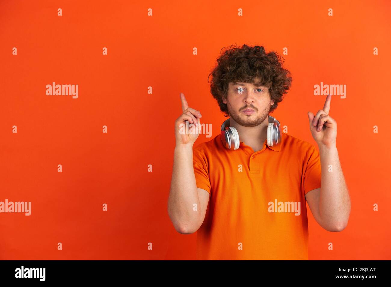 Pointing, choosing. Caucasian young man's monochrome portrait on orange ...