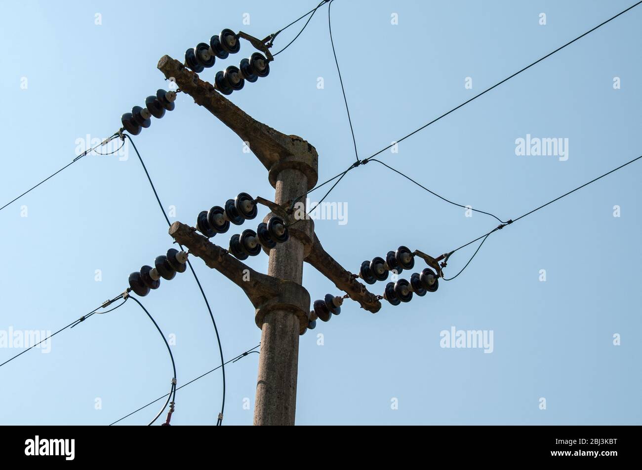 a cement pylon of an overhead power line with black glass insulators ...