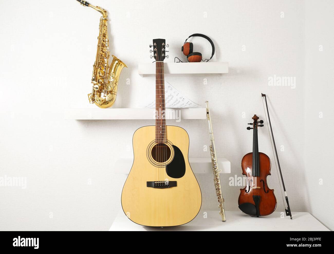Musical instruments and headphones on decorated shelves against white ...