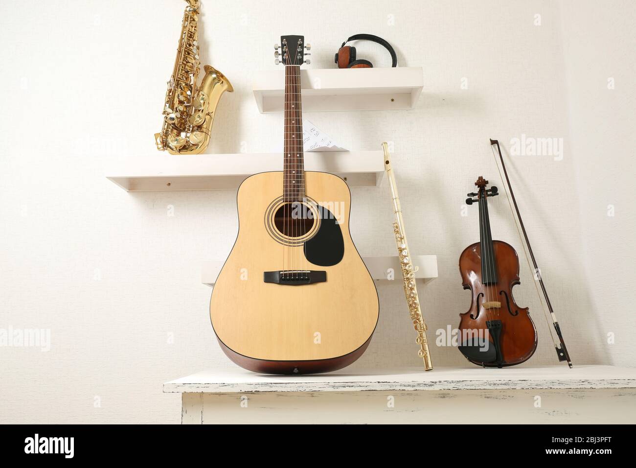 Musical instruments and headphones on decorated shelves against white ...