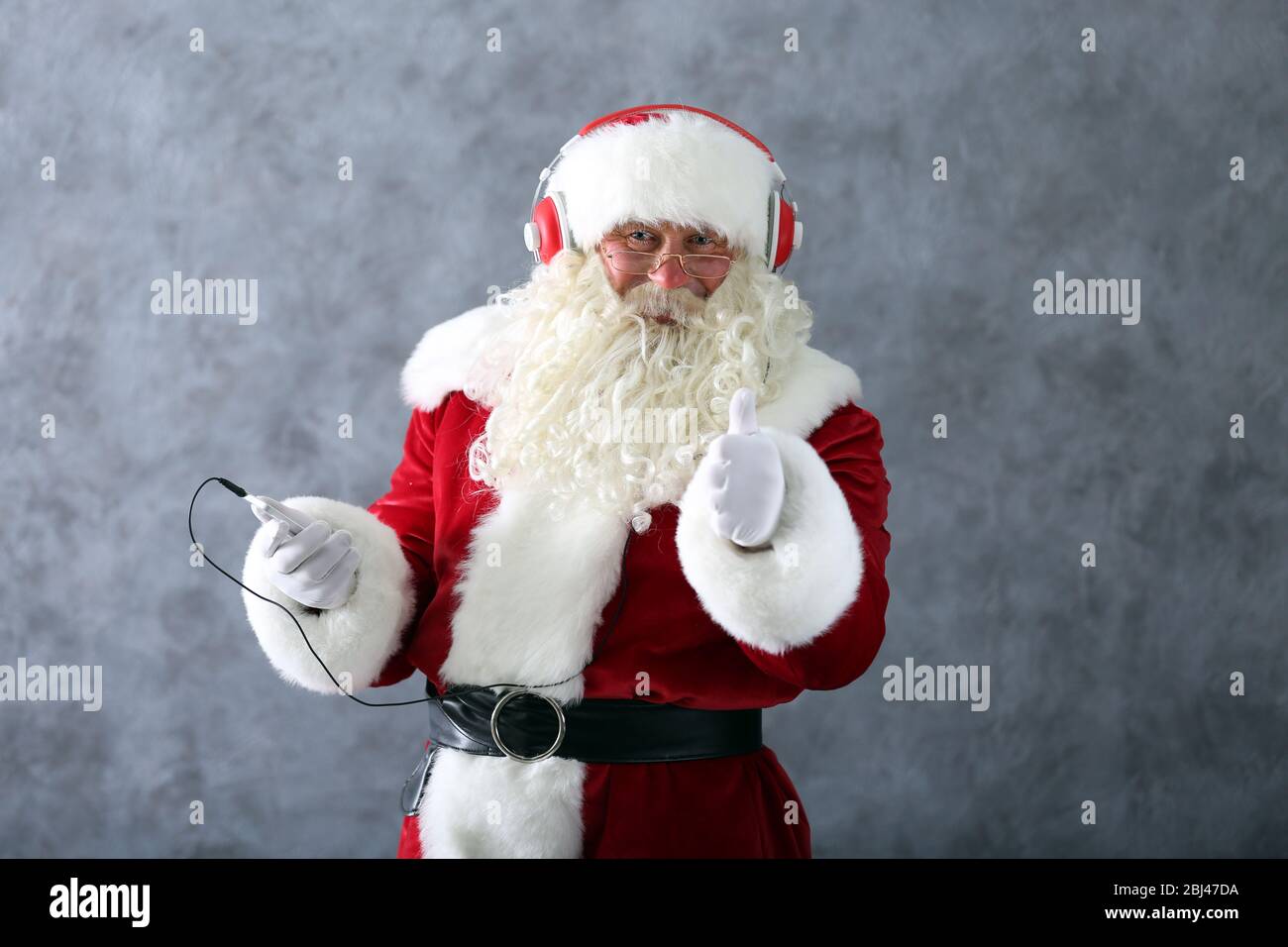 Santa Claus with headphones listening to music on gray wall background ...