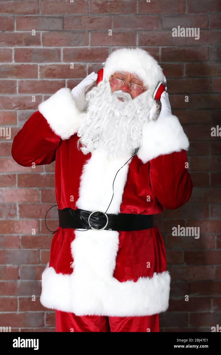 Santa Claus with headphones listening to music on brick wall background ...