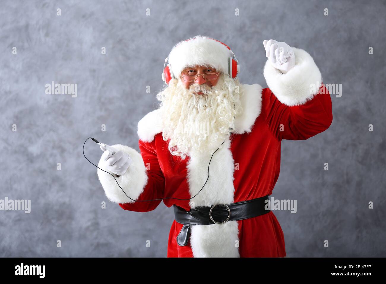 Santa Claus with headphones listening to music on gray wall background ...