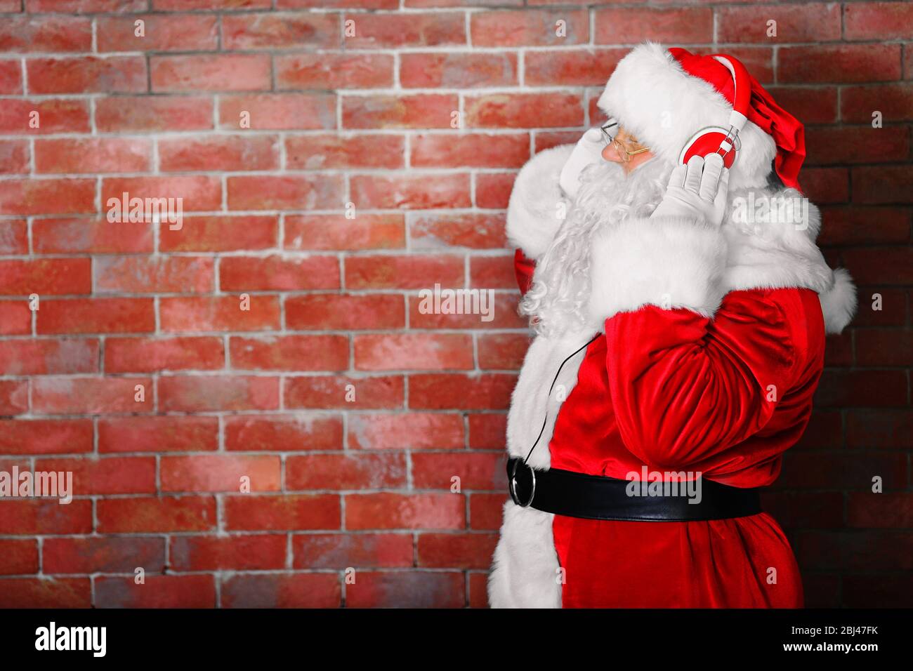 Santa Claus with headphones listening to music on brick wall background ...