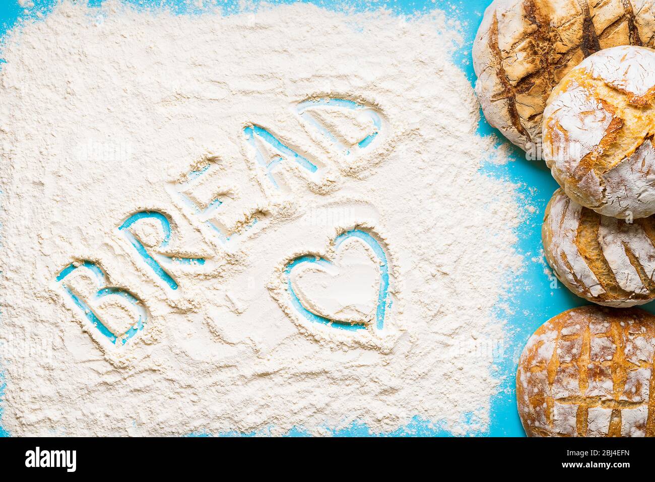 The word bread wrote in the flour spread on a blue table. Pile of round ...