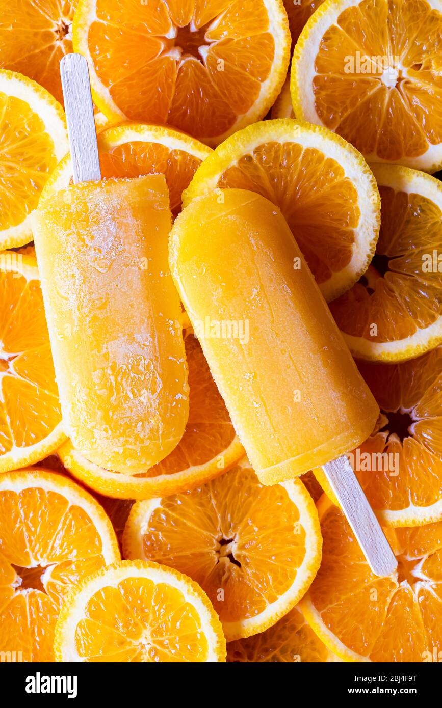 Two orange ice cream on stick and slices of fresh oranges. Fruitty ice ...