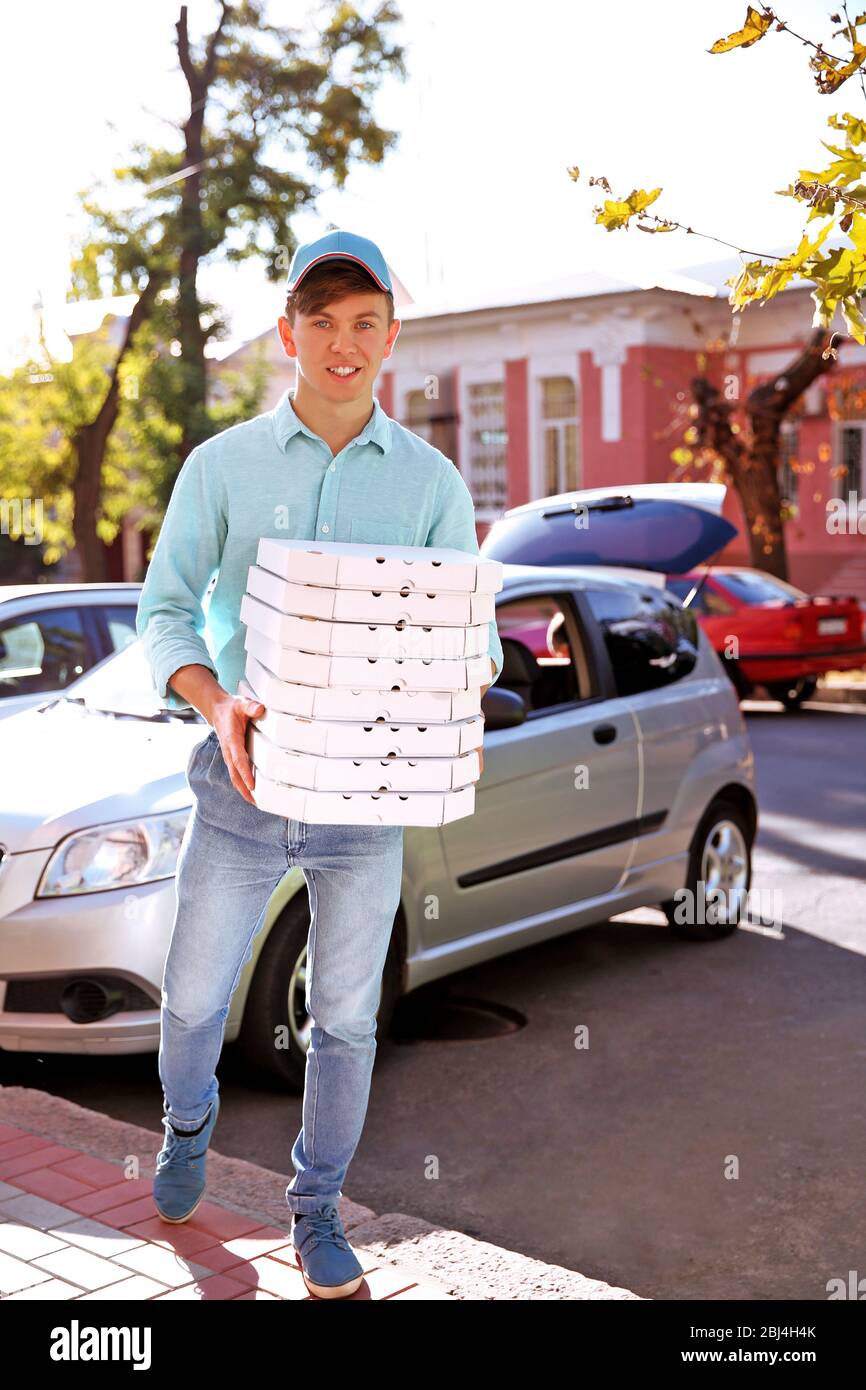 Pizza delivery boy holding boxes with pizza near car Stock Photo - Alamy