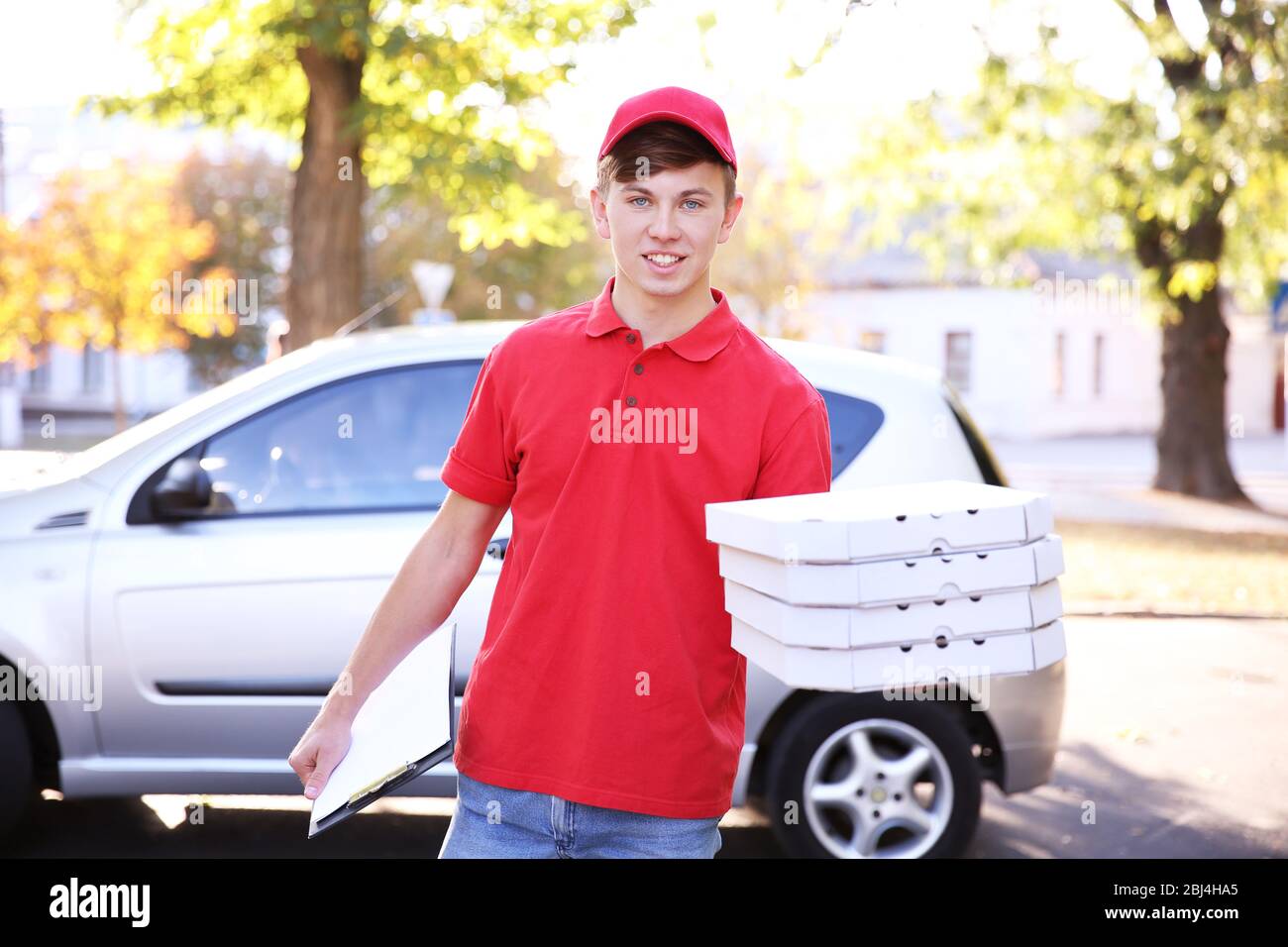 Pizza delivery boy holding boxes with pizza near car Stock Photo - Alamy