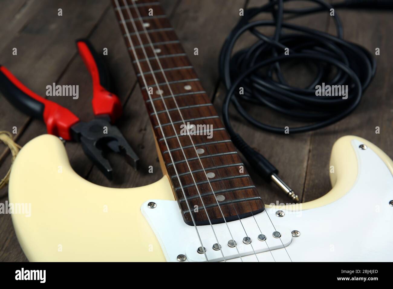 Electric guitar with pliers and cords on wooden background, close up ...