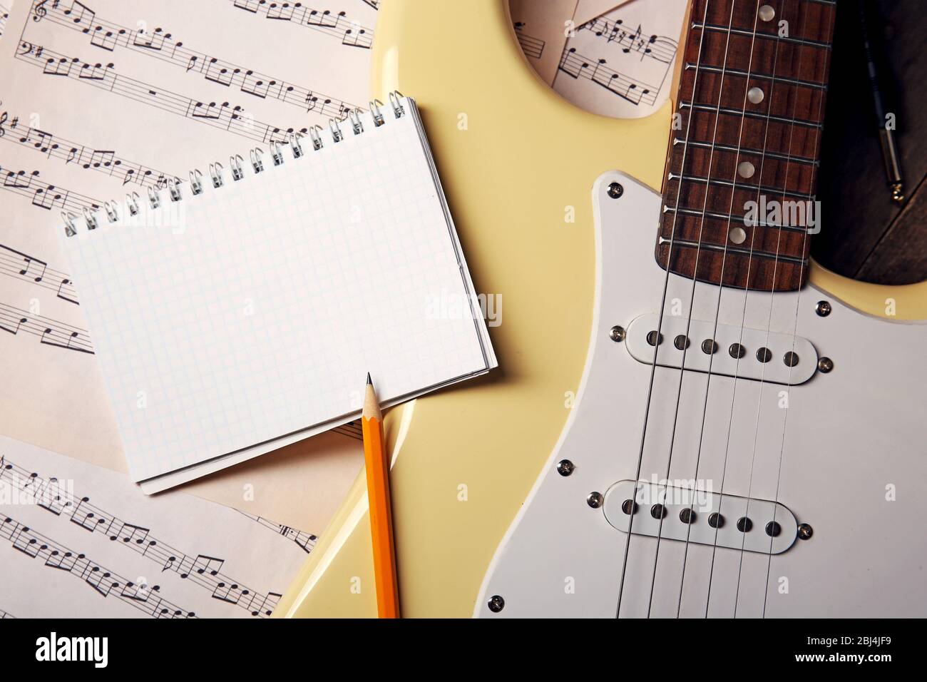 Electric guitar with notebook and pencil on musical notes background ...