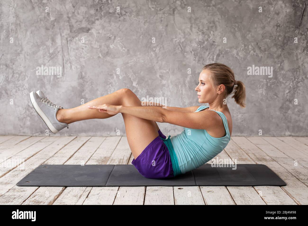 Young woman lays on carpet and doing crunches with outstretched arms ...