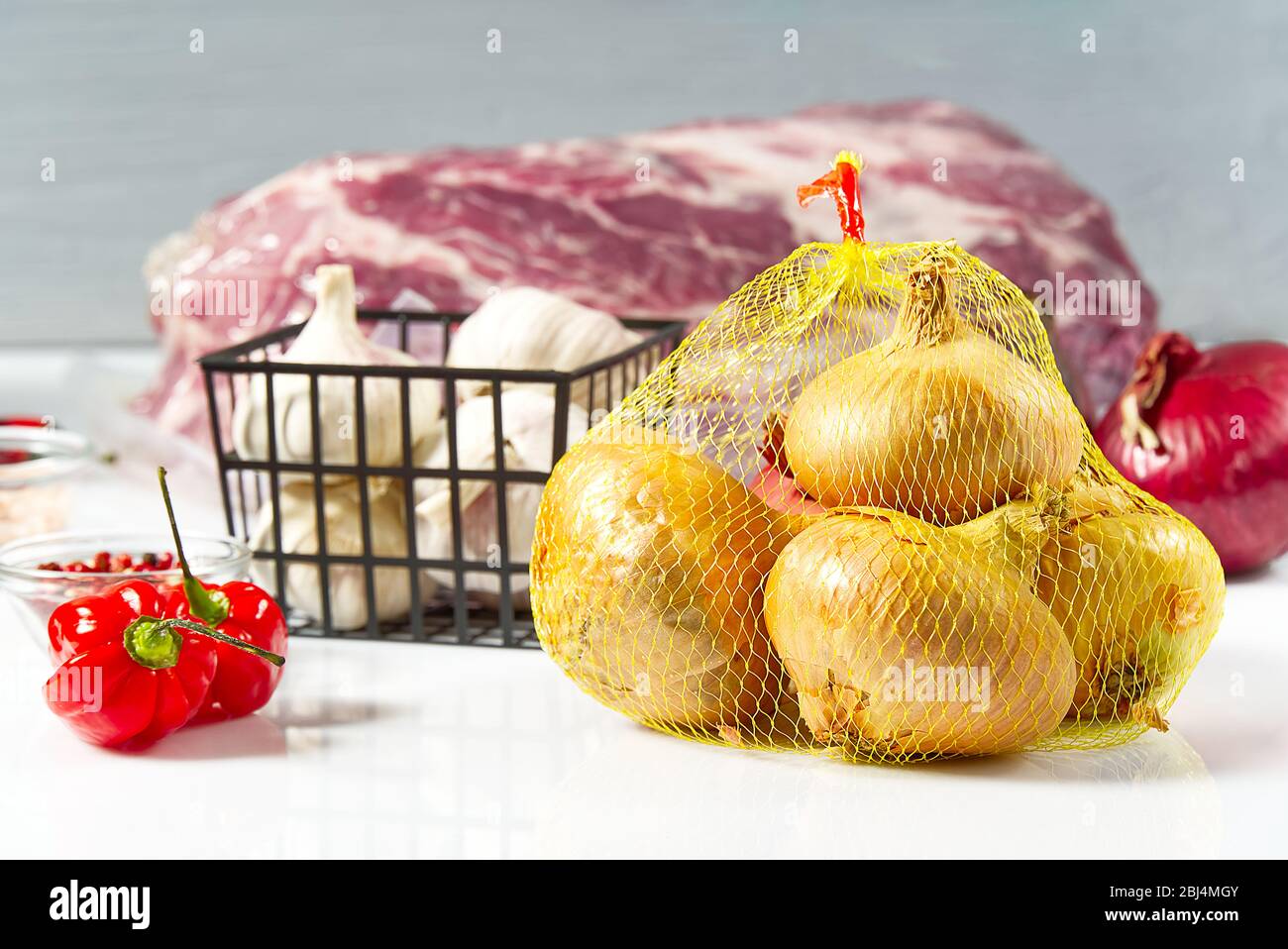 bag of onions on white table. with garlic and raw pork meat in vacuum ...
