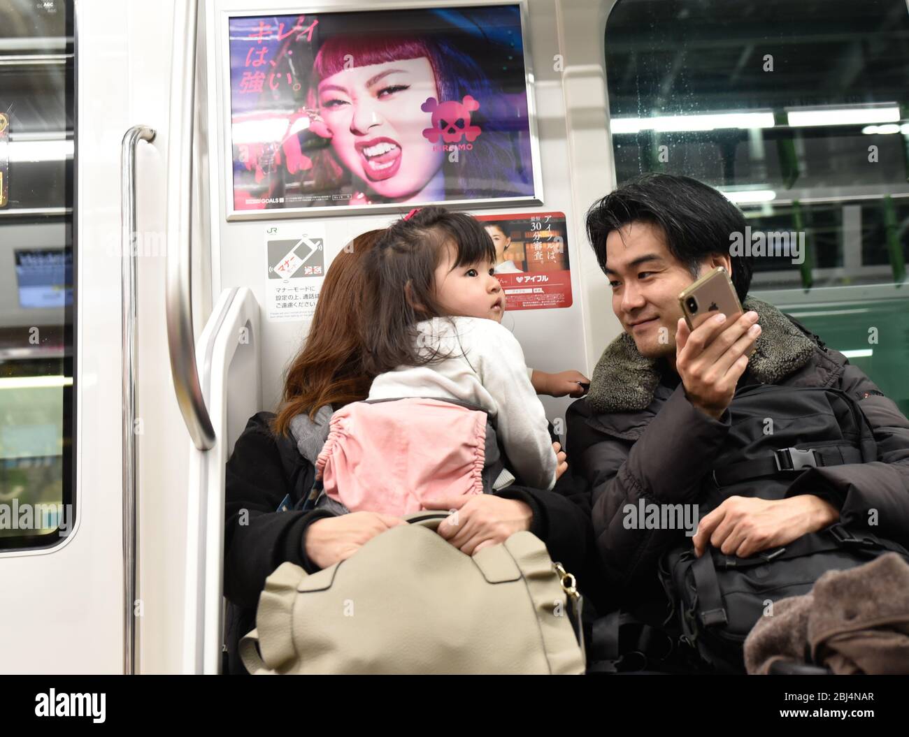Parents with their young toddler taking a train ride back home and using their smartphone to ...