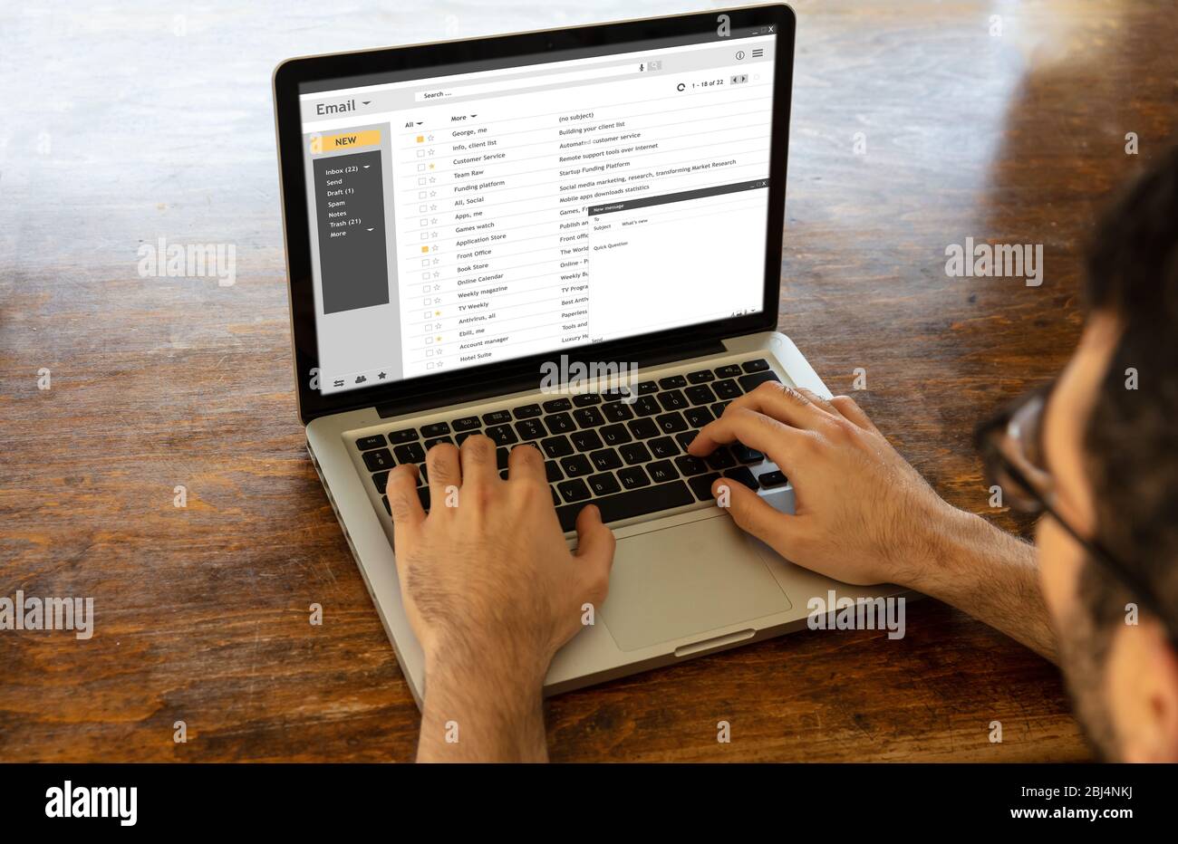 Email inbox message list on a computer screen, man working with a laptop, wooden office desk ...