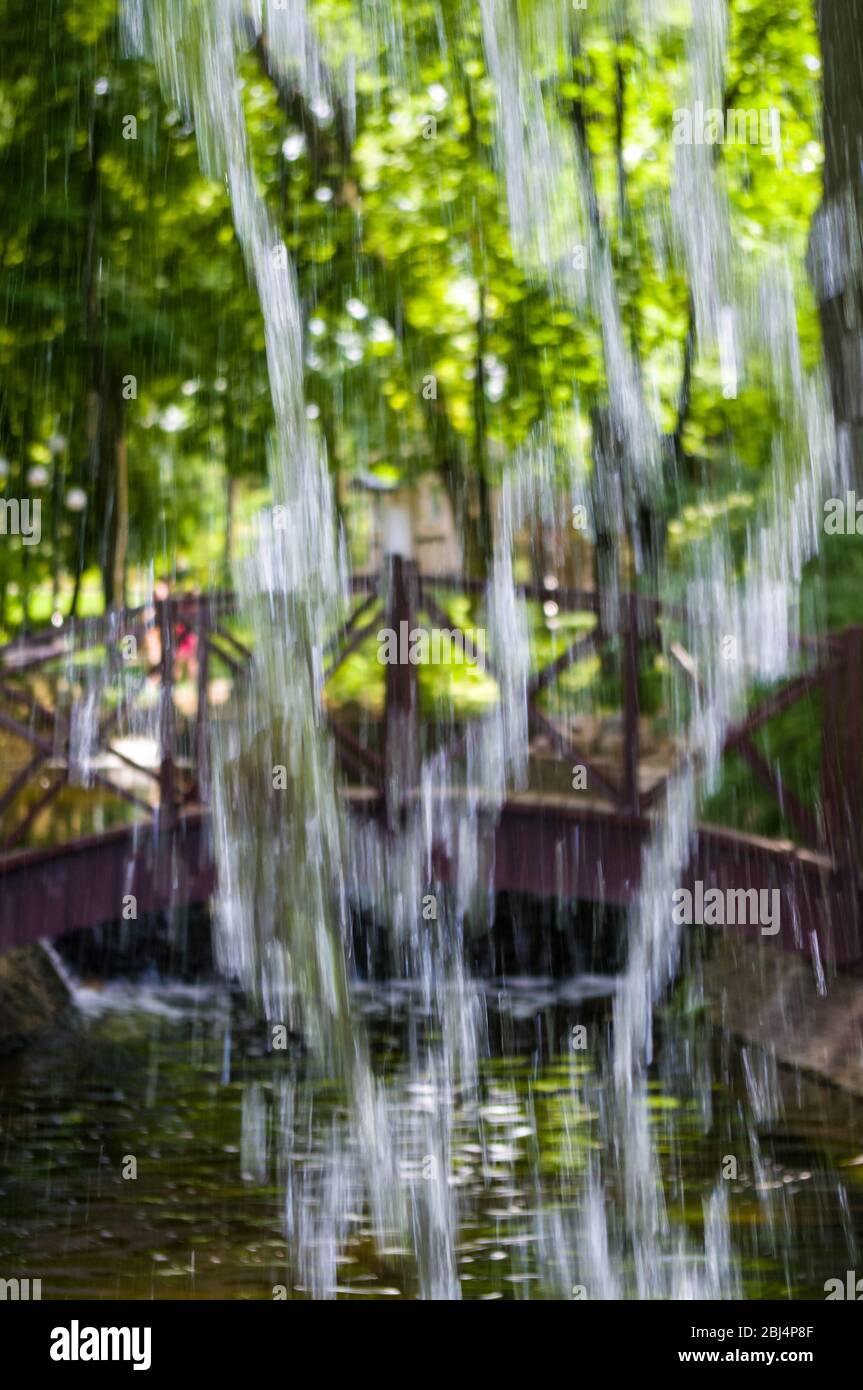 transparent falling water vertical flows against a blue sky and green ...