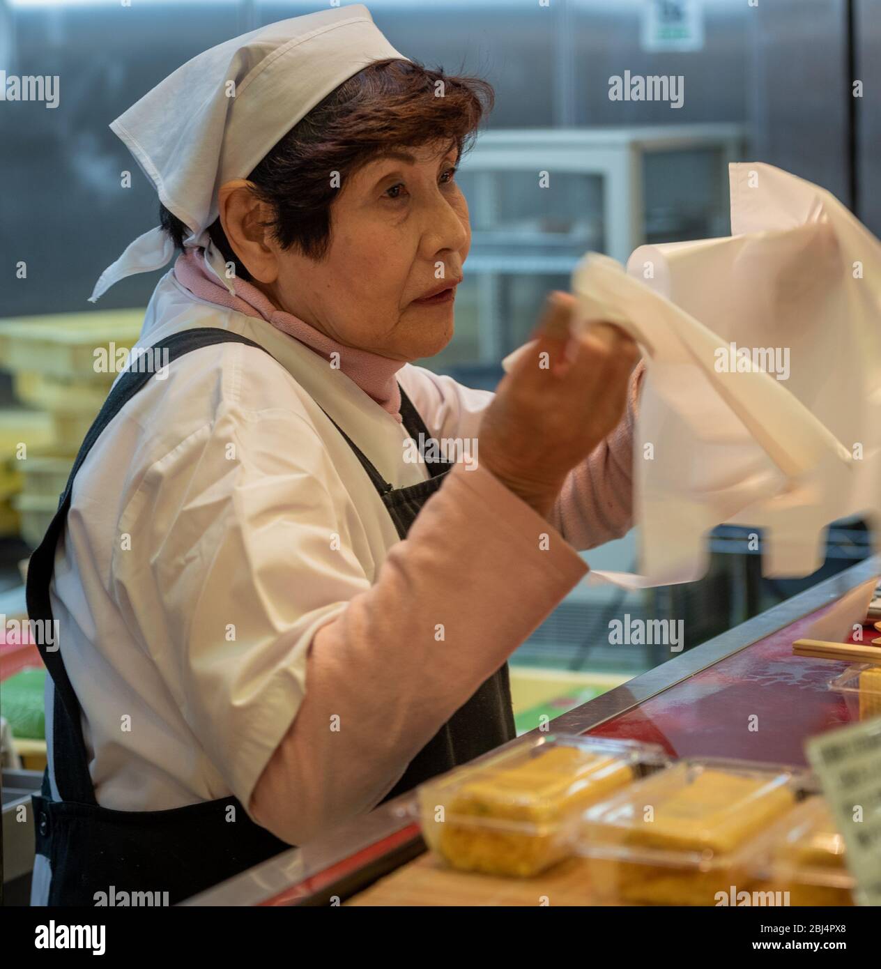 A seller at the Nishiki food market in Kyoto Japan offering food for ...