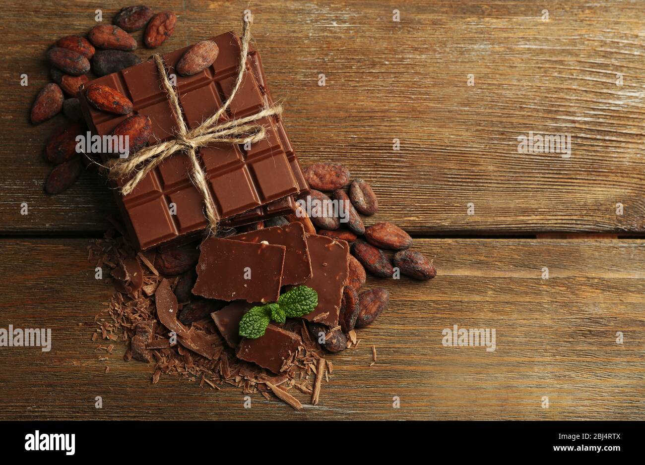 Chocolate pieces, shavings and cocoa beans on color wooden background ...
