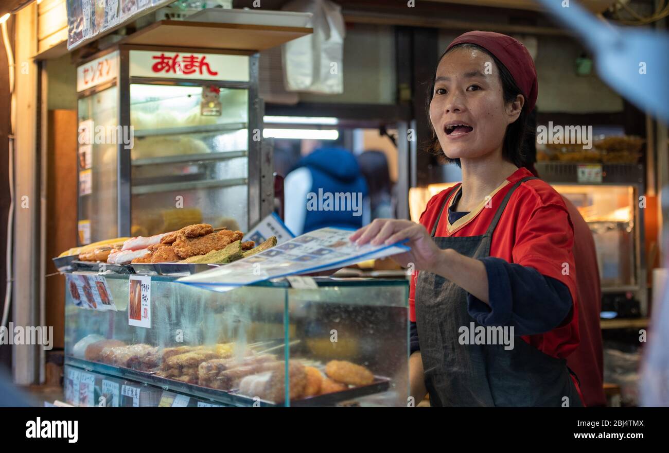 A young woman showing her food menu to tourists that pass by ...