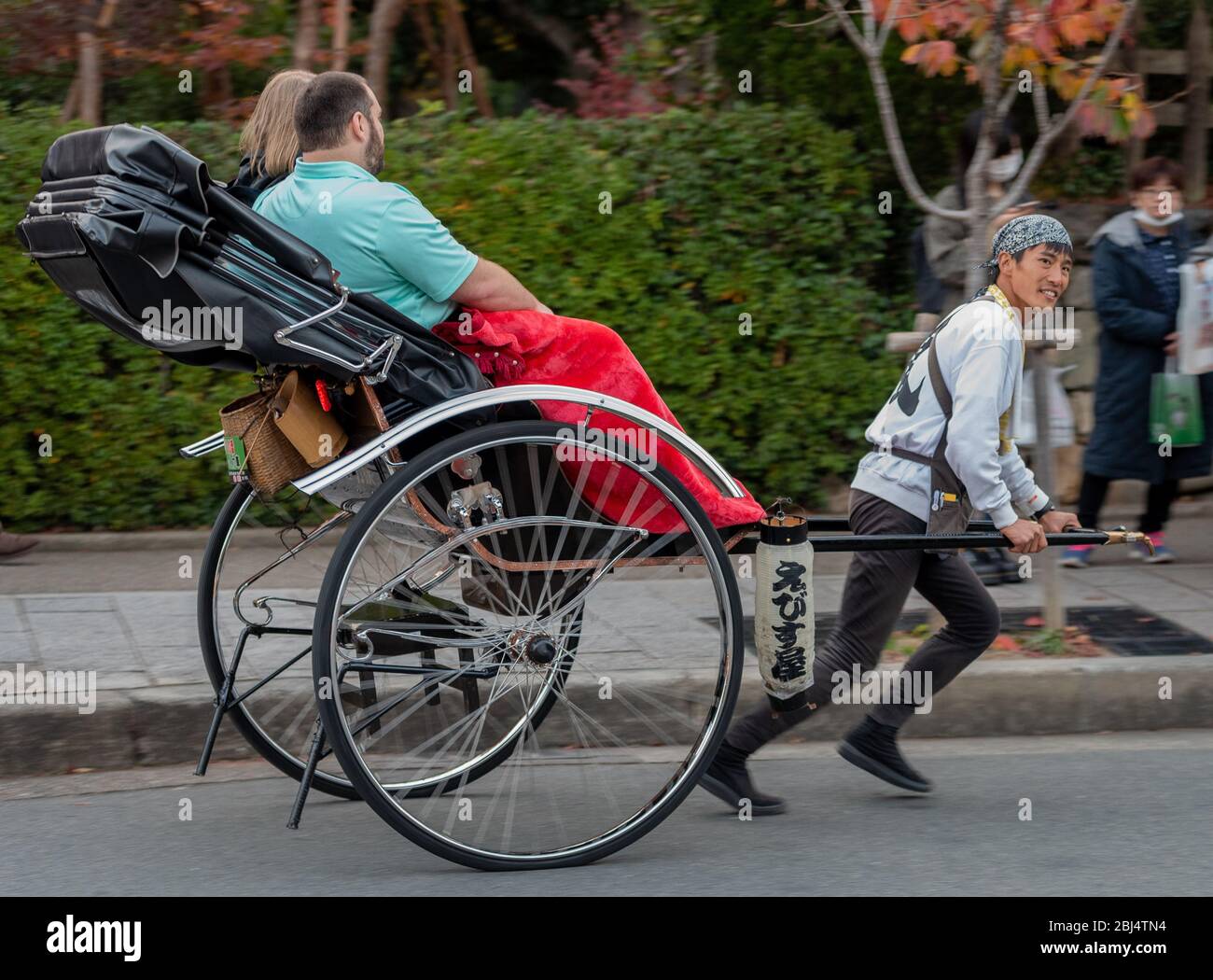 A young rickshaw driver is pulling two tourists in Arashiyama, Kyoto ...