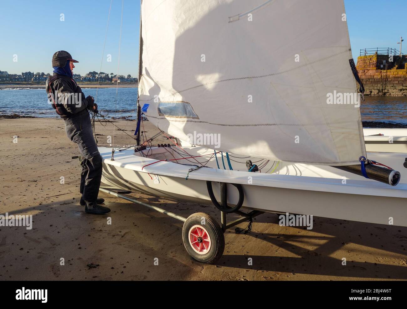 Man hoisting sail on sailing dinghy, in preparation for club racing ...