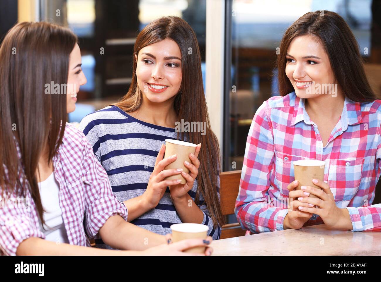 Three smiling friends speaking with coffee in hands Stock Photo - Alamy