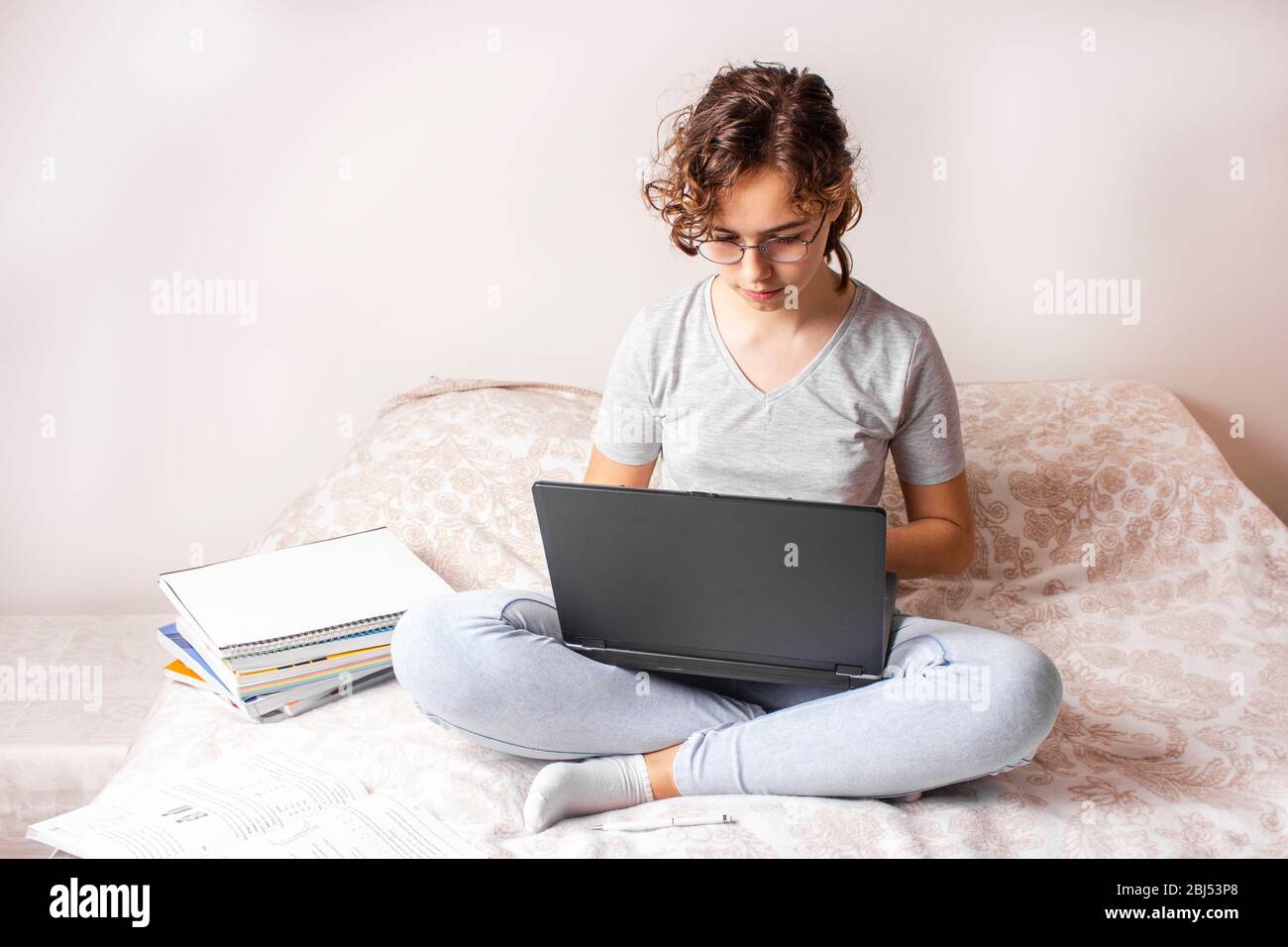 Pretty curly teenager girl studying online on her bed with lap top ...