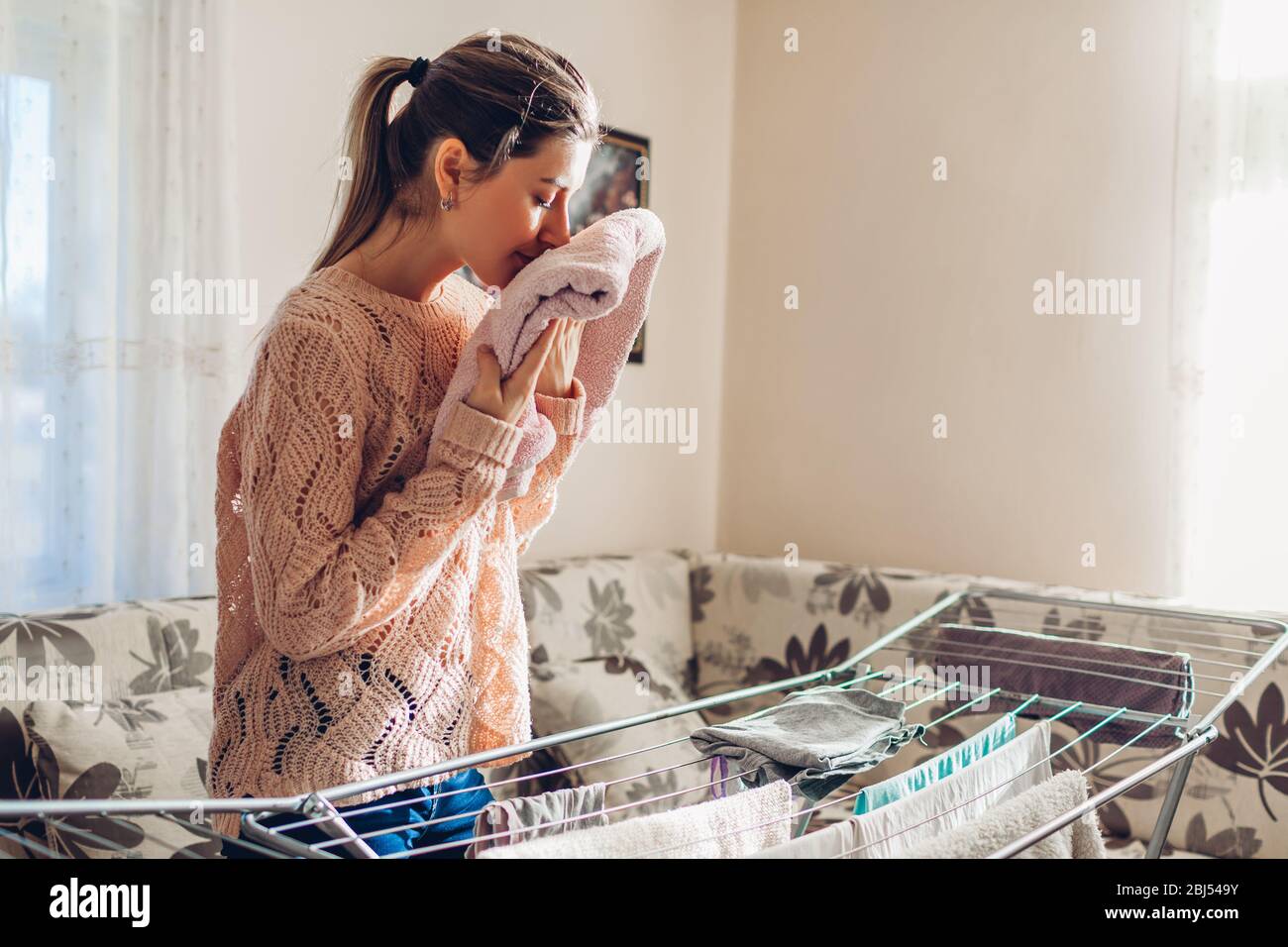 Happy woman smelling gathered clean clothes from dryer in heap ...