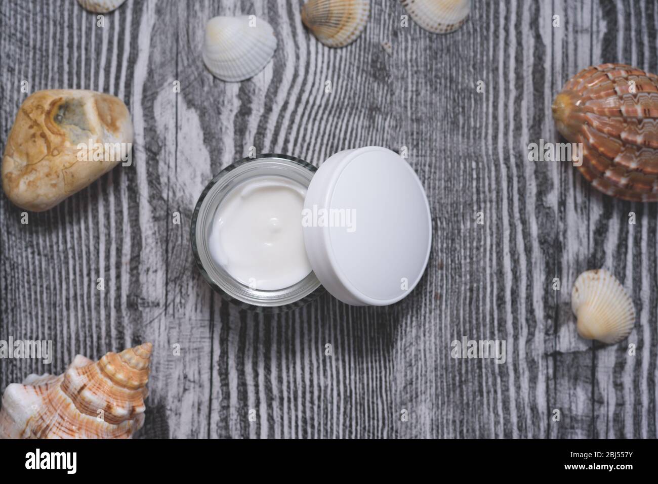Opened facial cream and sea shells and stone on the wooden background ...