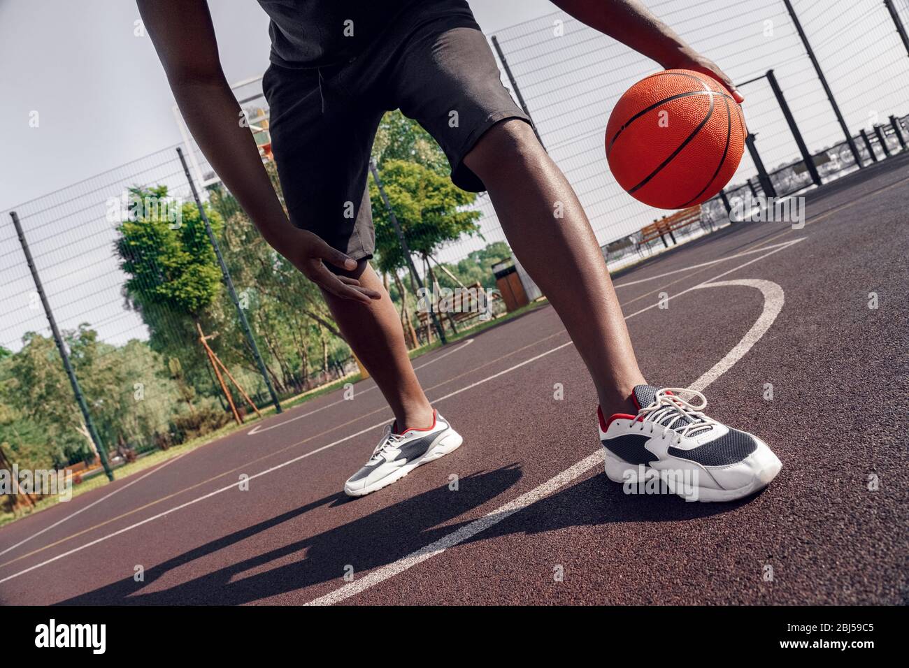 Outdoors Activity. African man playing on court dribbling ball between ...