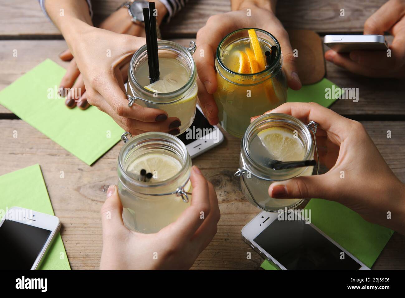 Four hands with smart phones holding cocktails, on wooden table ...