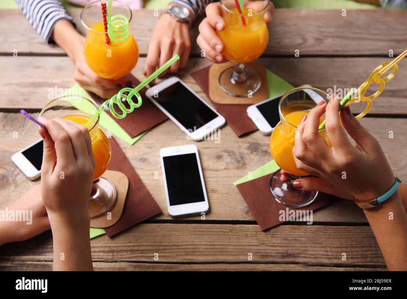 Four hands with smart phones holding cocktails, on wooden table ...