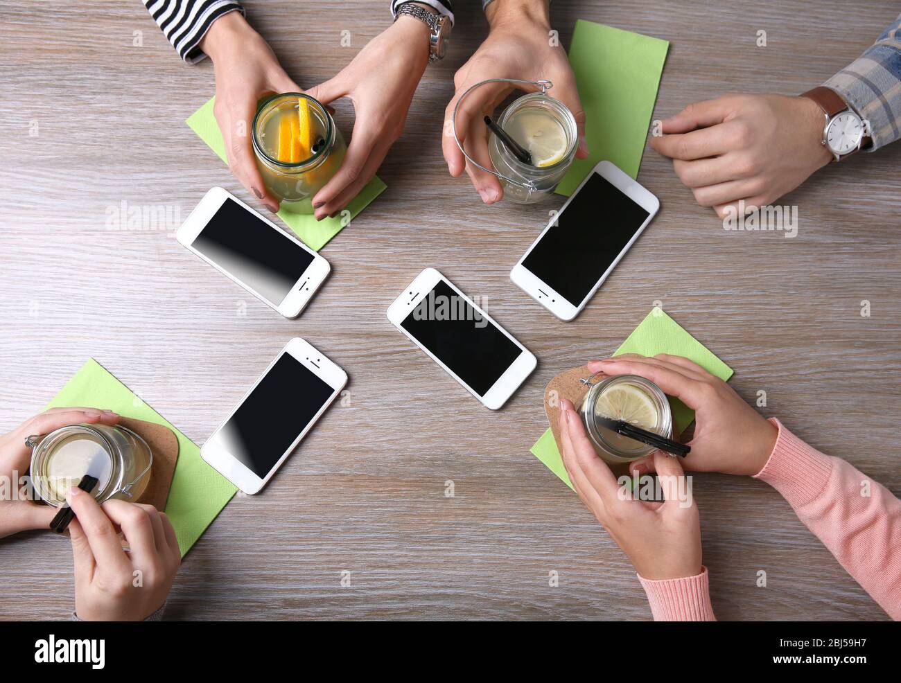 Four hands with smart phones holding cocktails, on wooden table ...