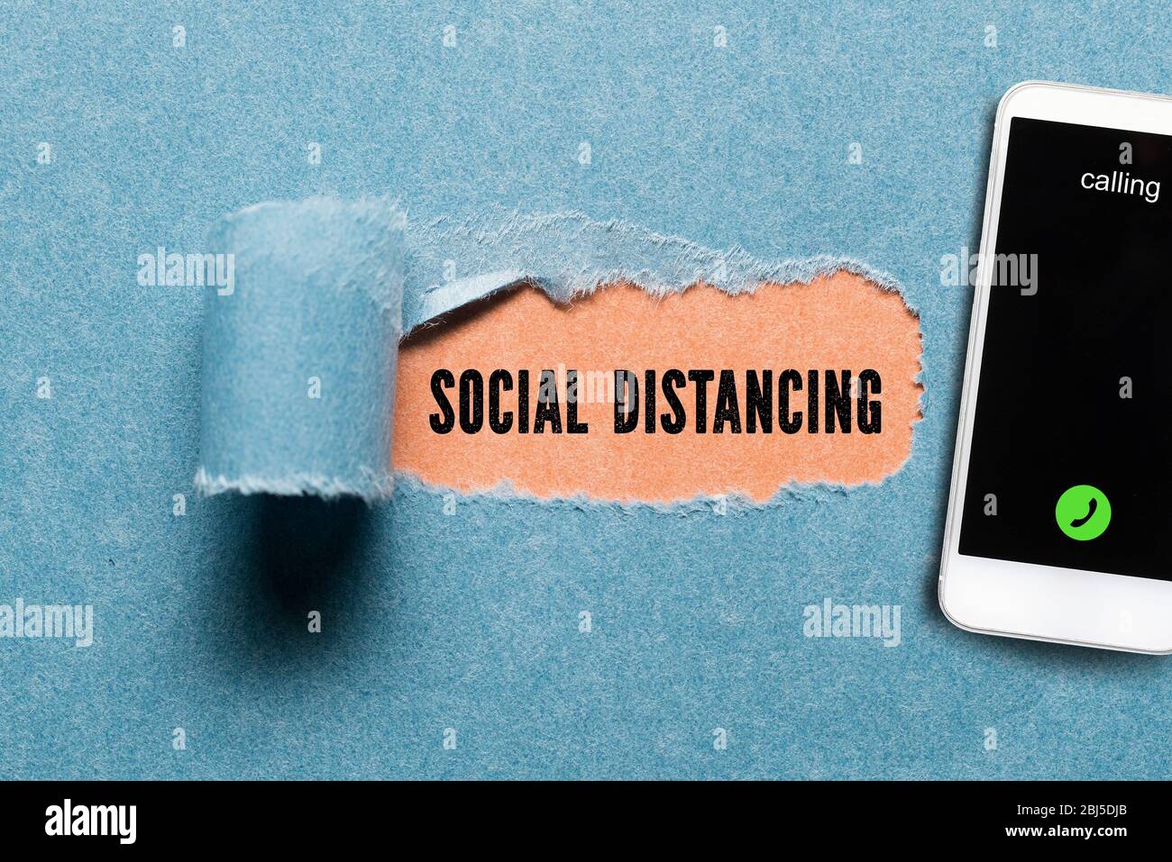 torn paper revealing message SOCIAL DISTANCING beside a smartphone on ...